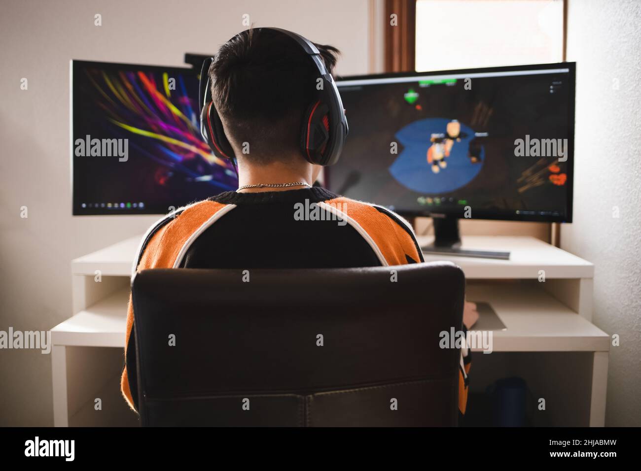 Back view of concentrated young gamer in headphones and glasses using ...