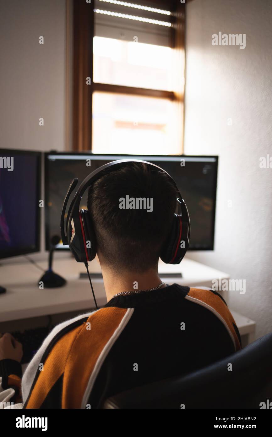 Back view of concentrated young gamer in headphones and glasses using ...