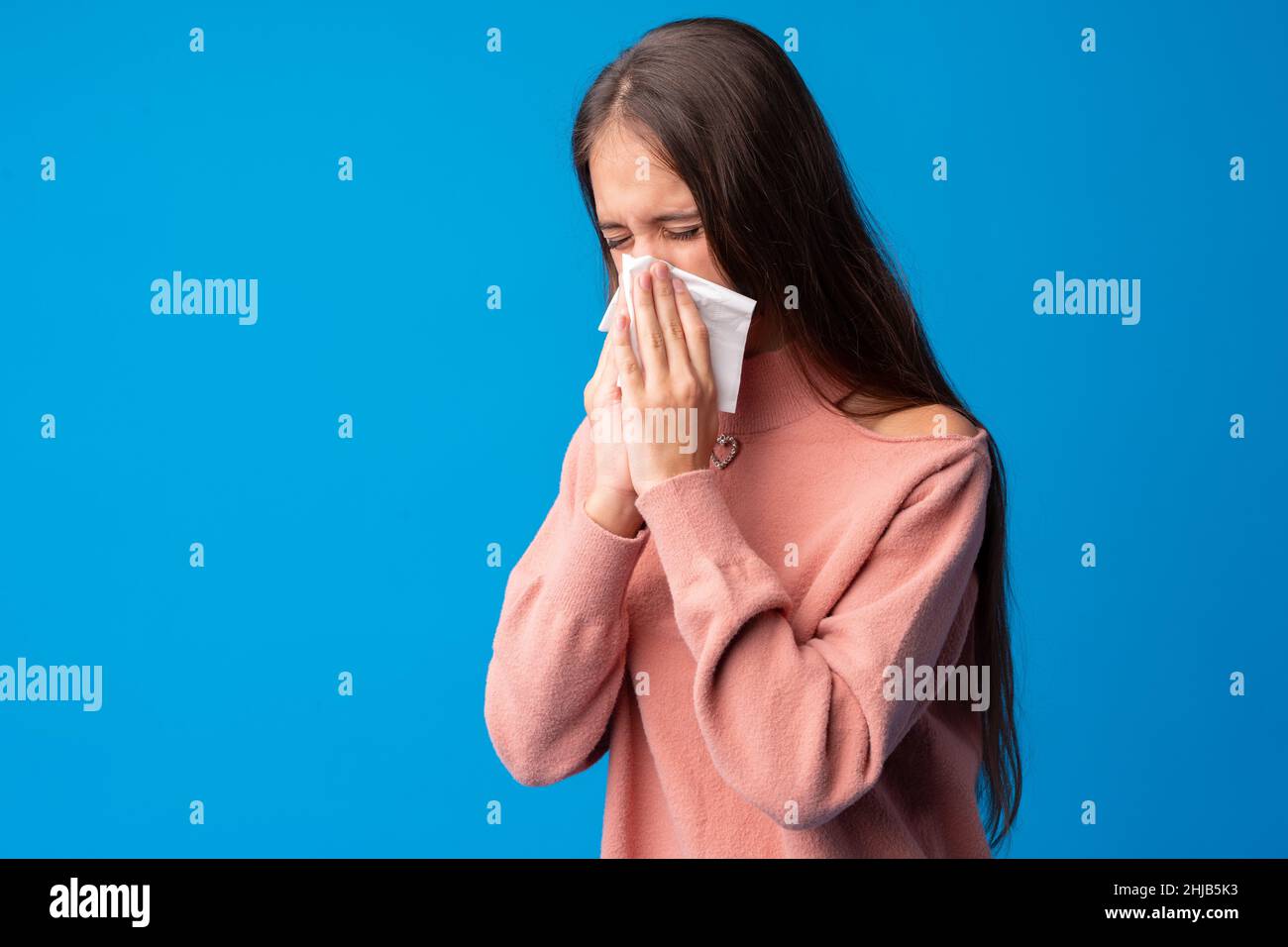 Teen girl blowing nose against blue background Stock Photo - Alamy