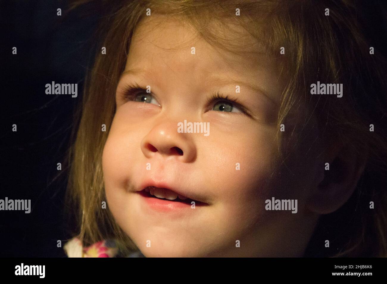 Face of child looking up and aside lighted by bright light in darkness ...