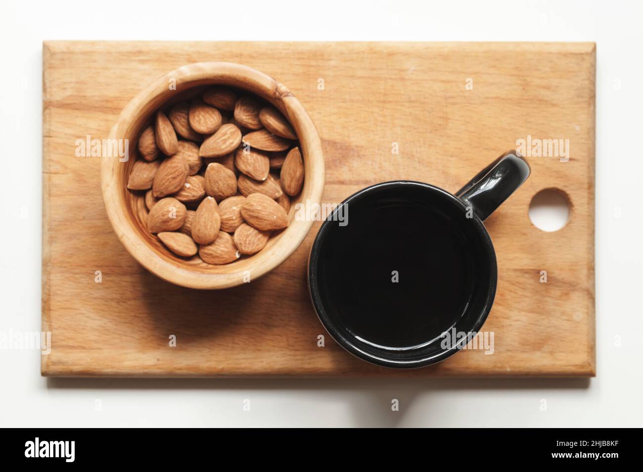 Cup of black coffee and a bowl of almond nuts stand on a wooden cutting ...