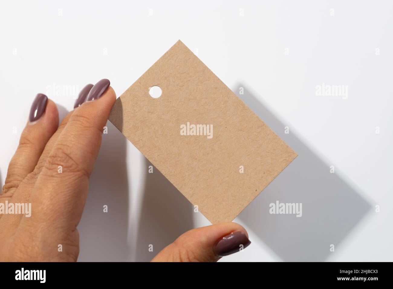Fingers holding cardboard blank rectangular label tag with small hole ...