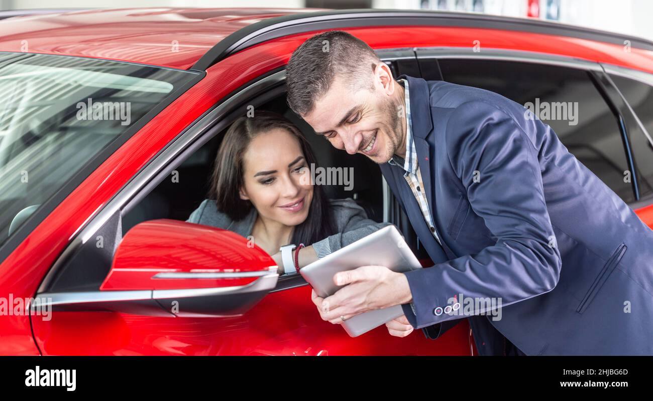 Car dealership employee with tablet shows woman intending to buy a red ...