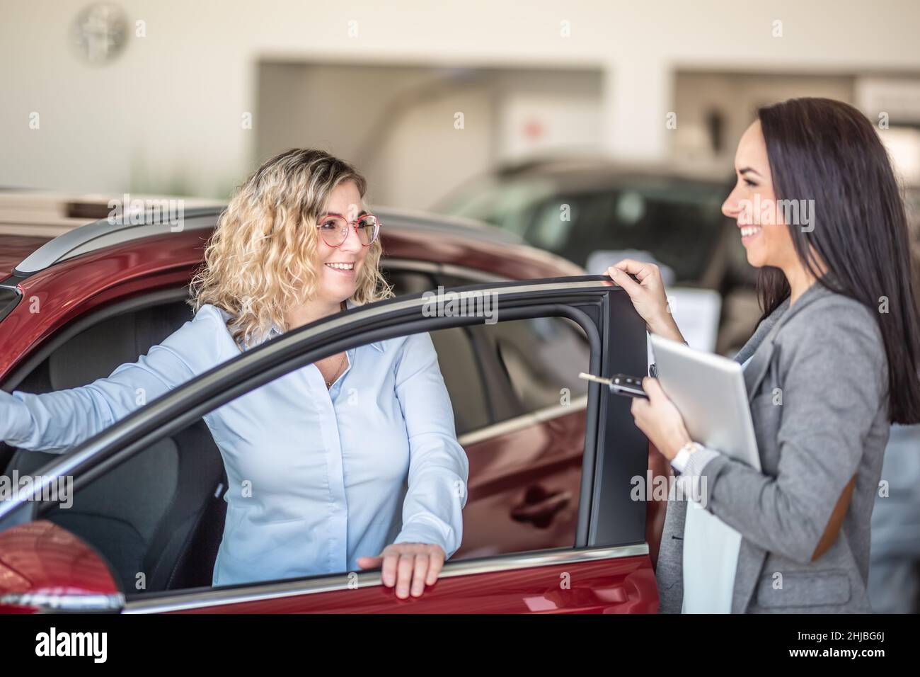 Female car seller and customer in automobile dealership are about to ...