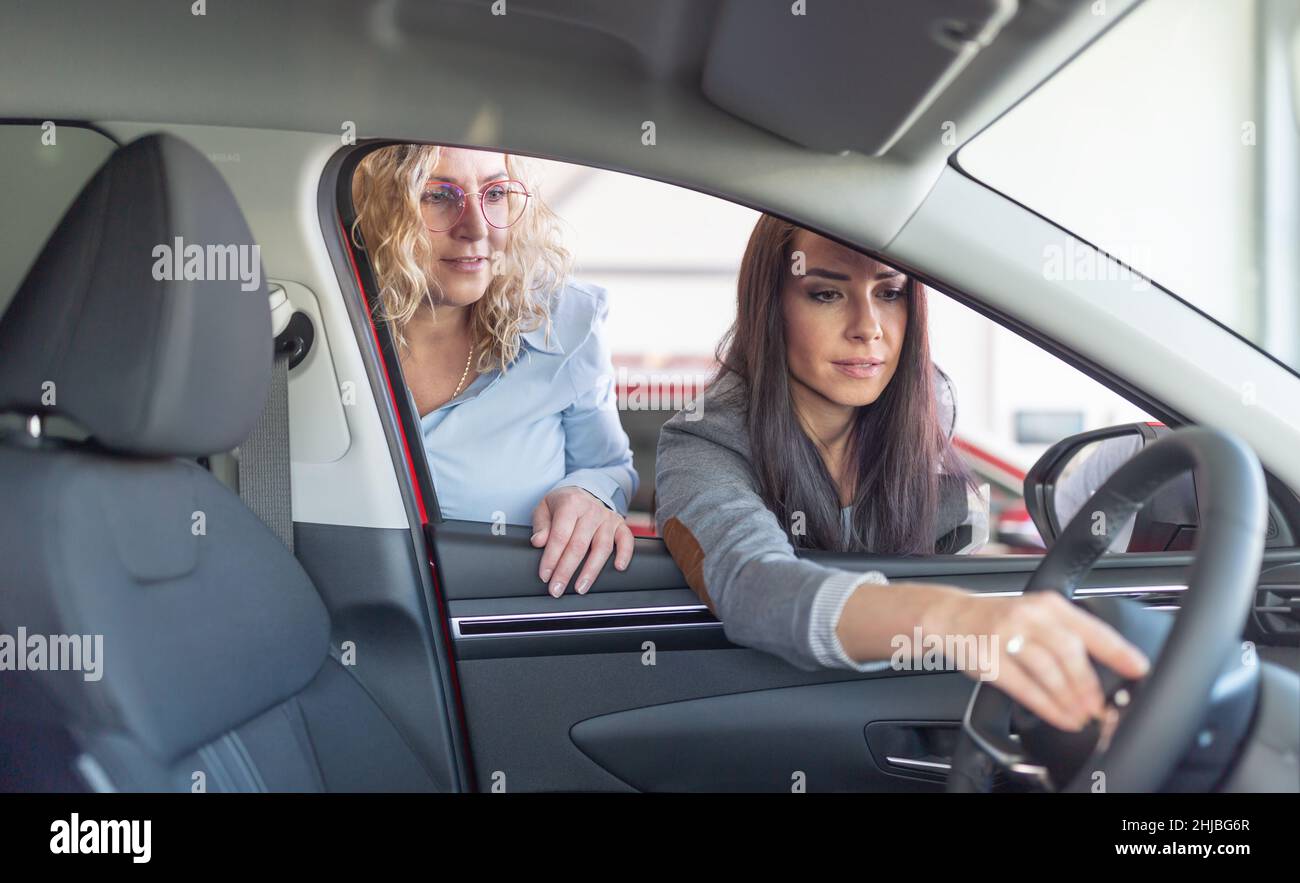Female car seller shows customer car interior in the dealership shop ...
