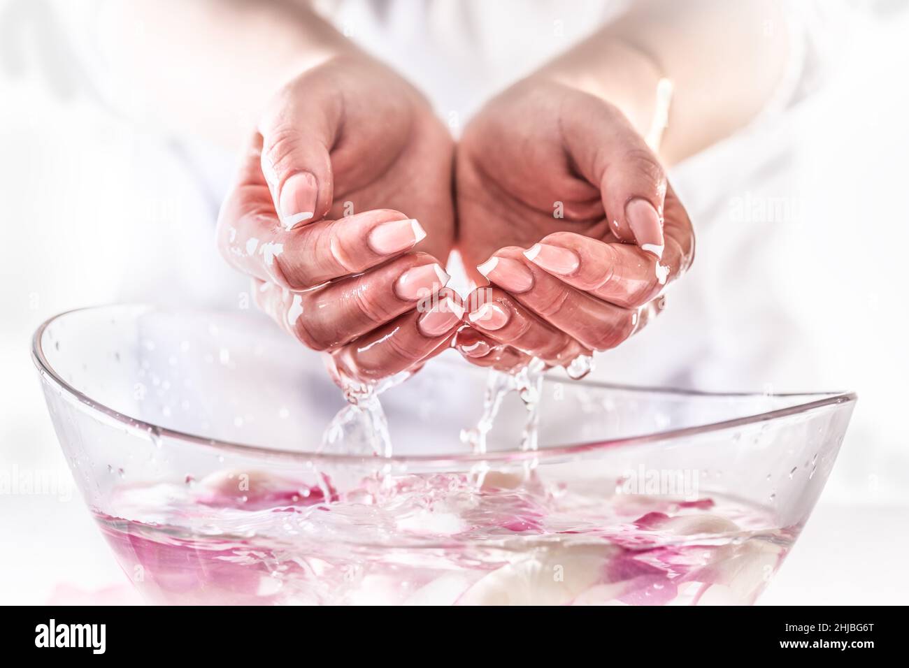 Detail of hand with perfect manicure raised from a glass bowl full of ...