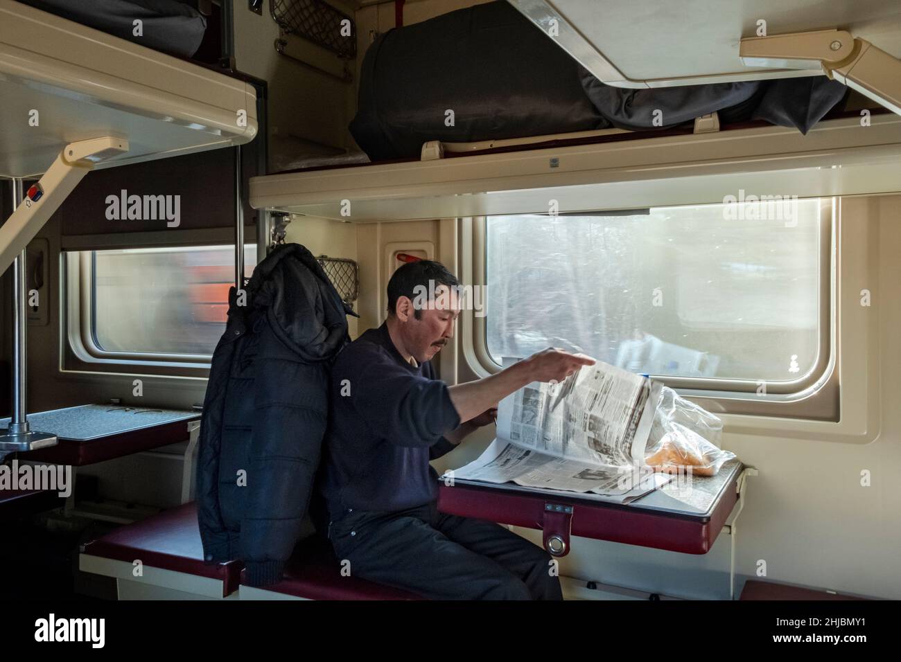 Daily life in Trans-Siberian Express. Passenger reads newspaper in the ...