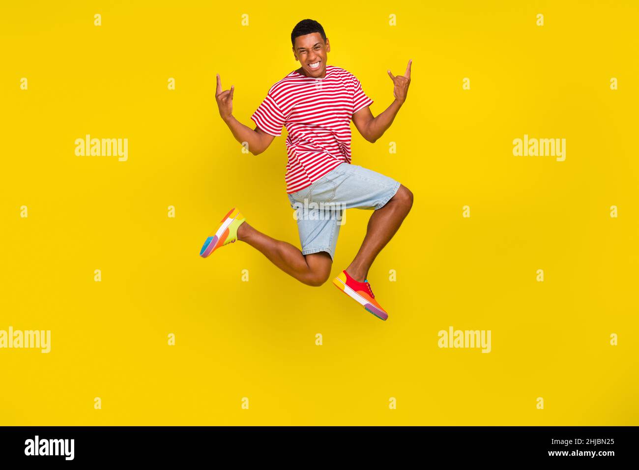 Full length photo of guy jump make horned punk sign wear striped t ...