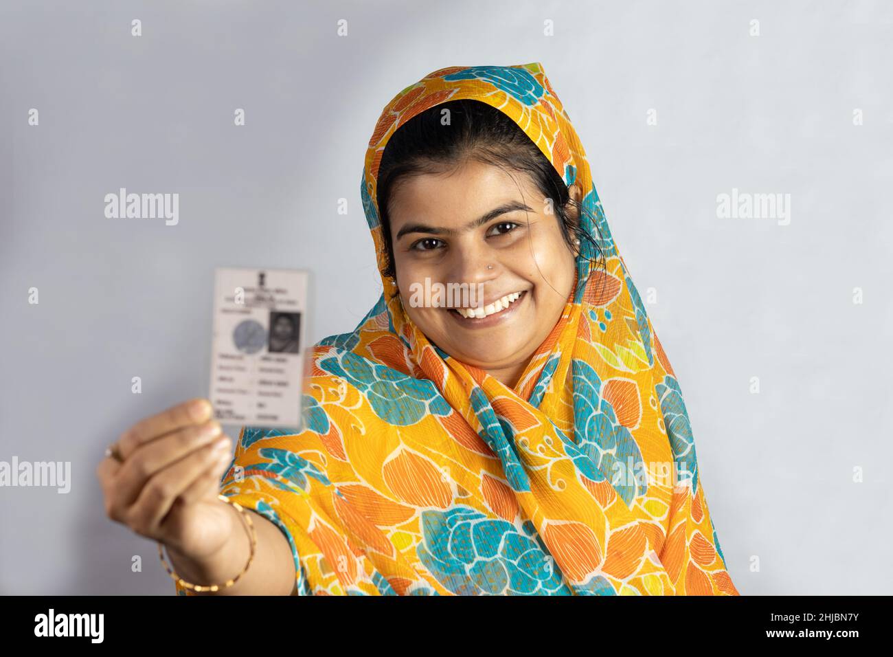 An Indian young woman smiling with voter card in hand on white ...