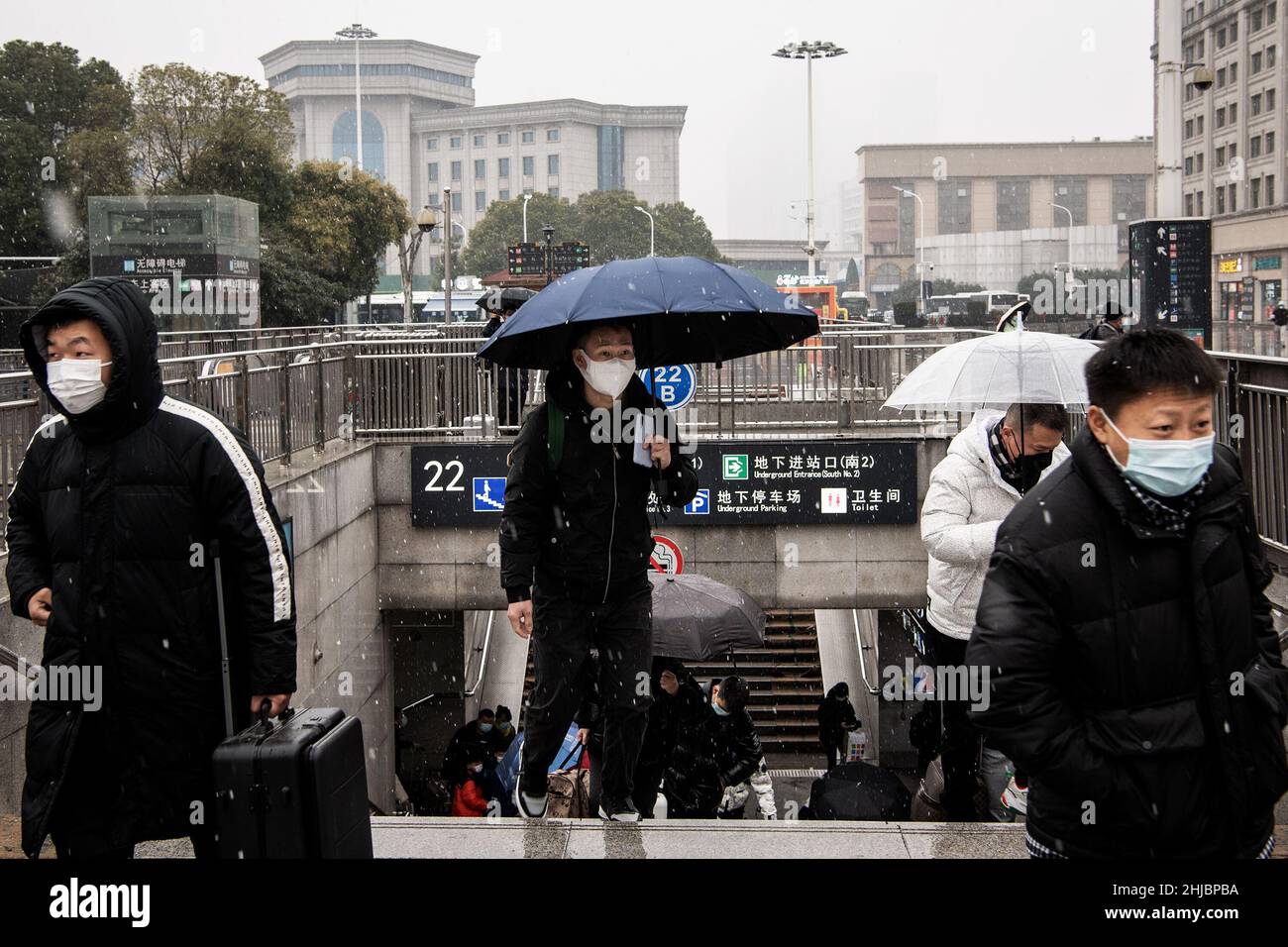 Wuhan, China. 28th Jan, 2022. Passengers wearing masks walk in snowfall ...
