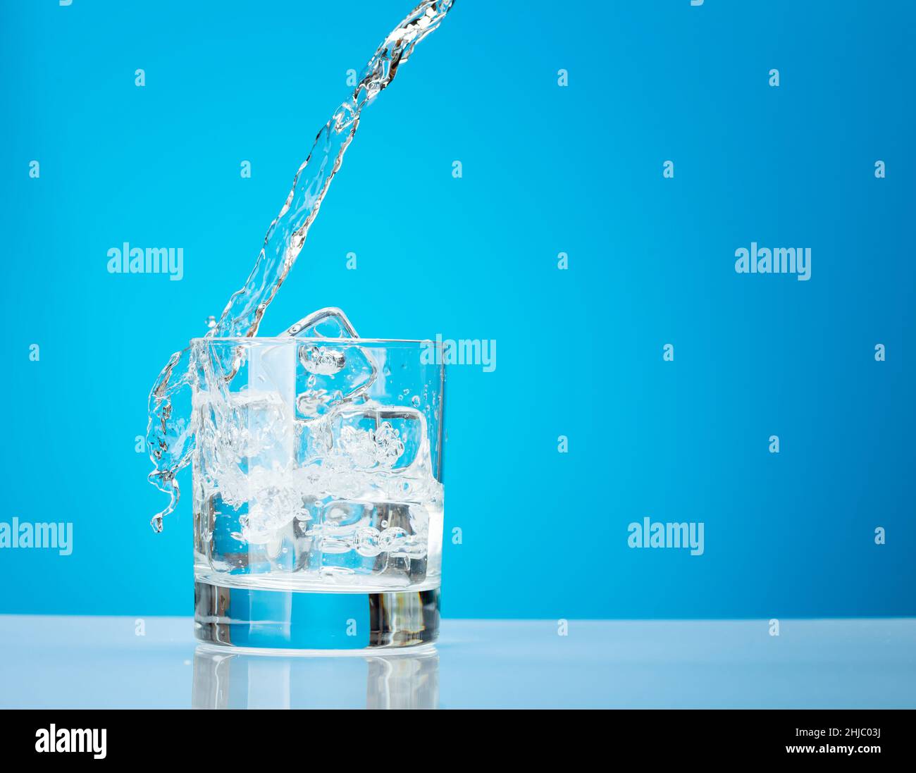 Fresh water pouring from bottle into glass with ice cubes over blue background Stock Photo - Alamy