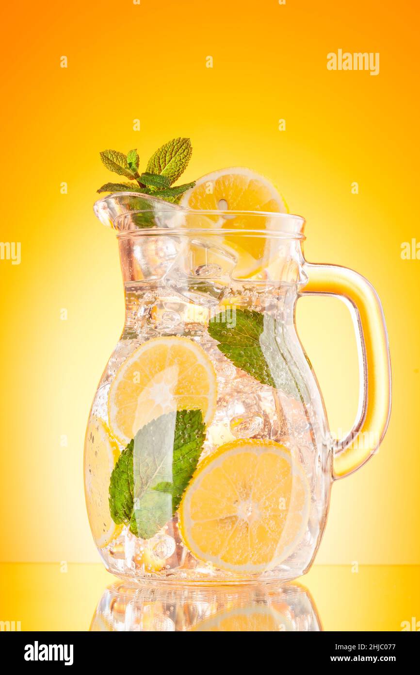 Lemonade pitcher with lemon, mint and ice cubes. Over yellow background ...