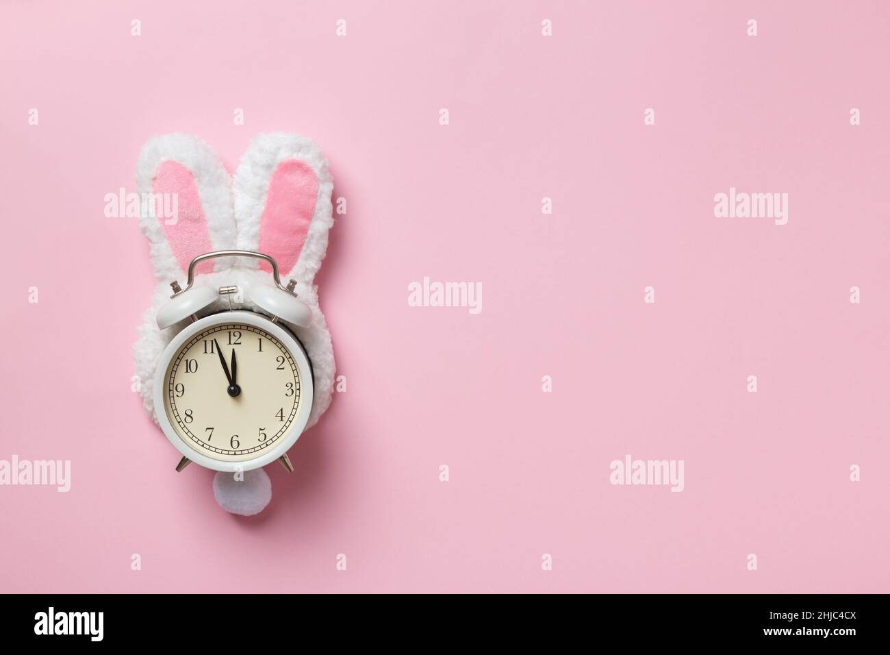 Alarm clock in easter bunny ears on a pink background with copy space ...