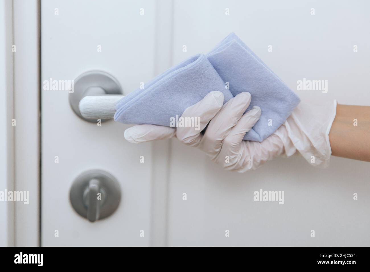 Cleaning door handle with blue wipe in white gloves. Sanitize surfaces ...
