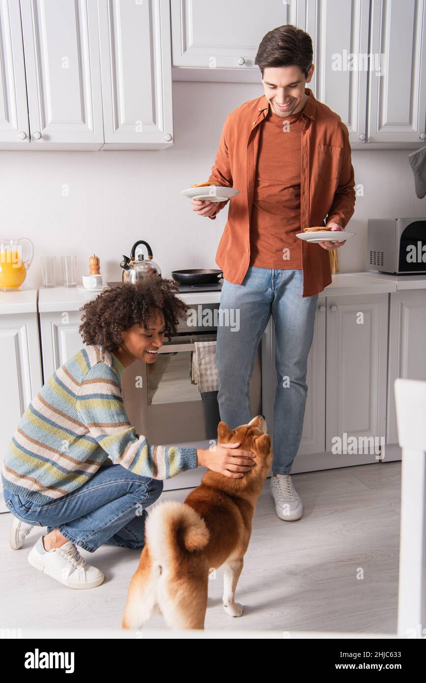 smiling african woman stroking shiba inu dog near boyfriend with ...