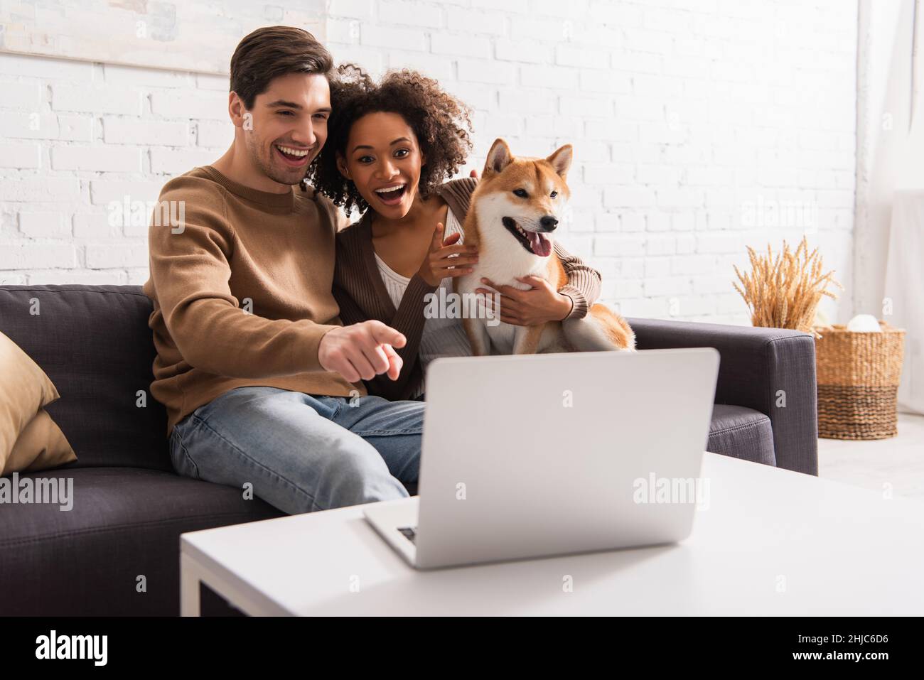 Positive man pointing at blurred laptop near african american ...
