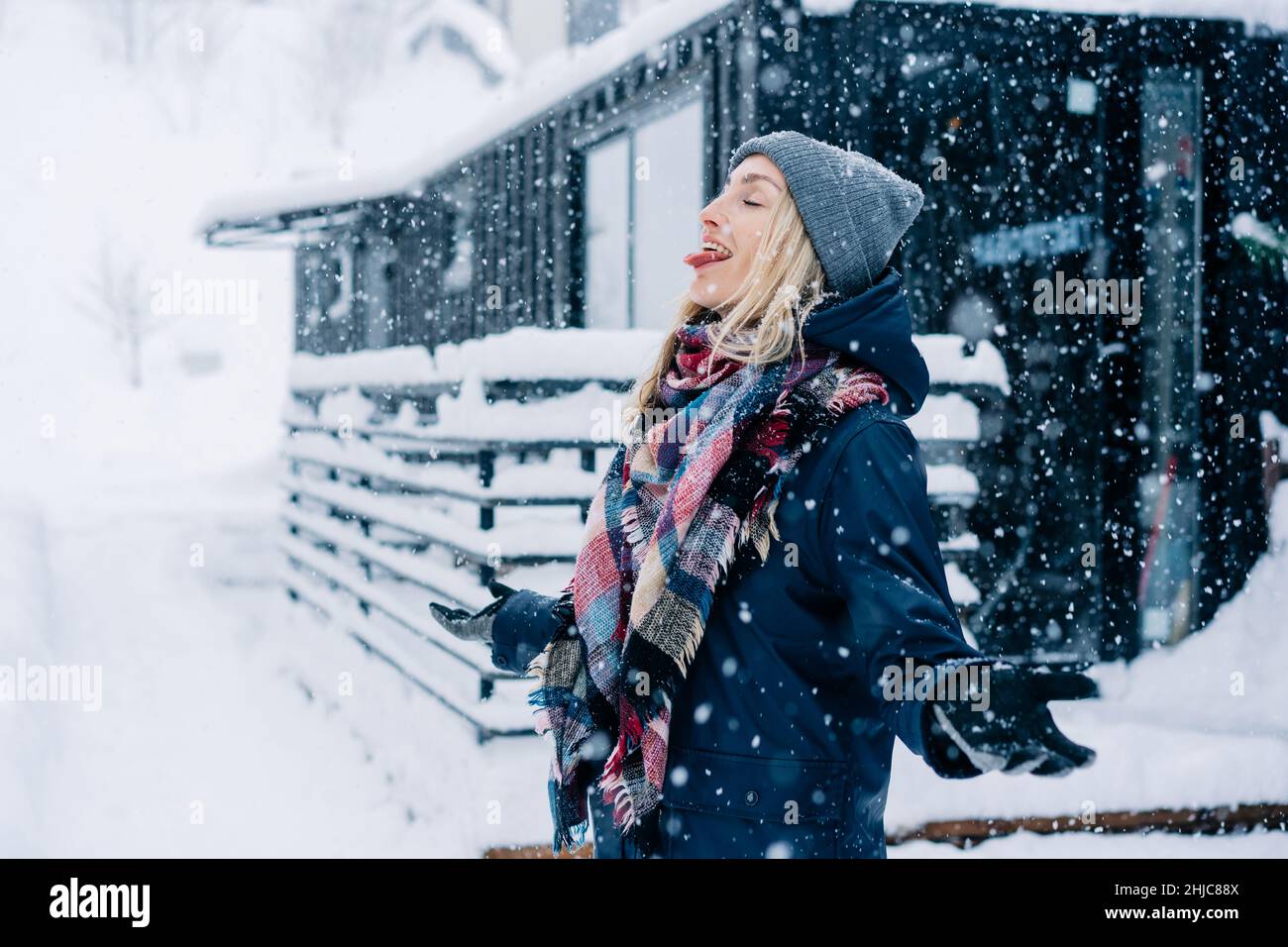 A young woman sticks out her tongue to catch snowflakes during a snow ...
