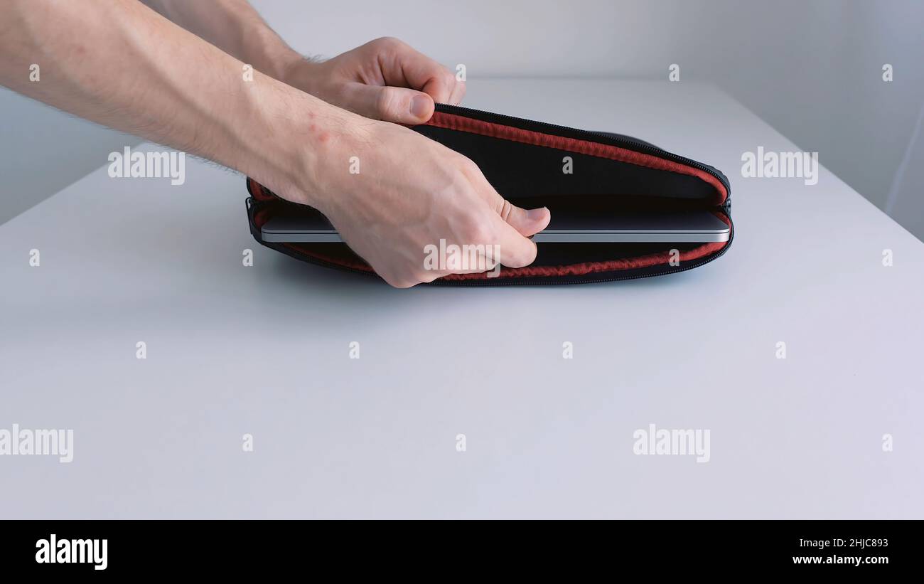 The guy putting small silver laptop into a bag and zipping it up on ...