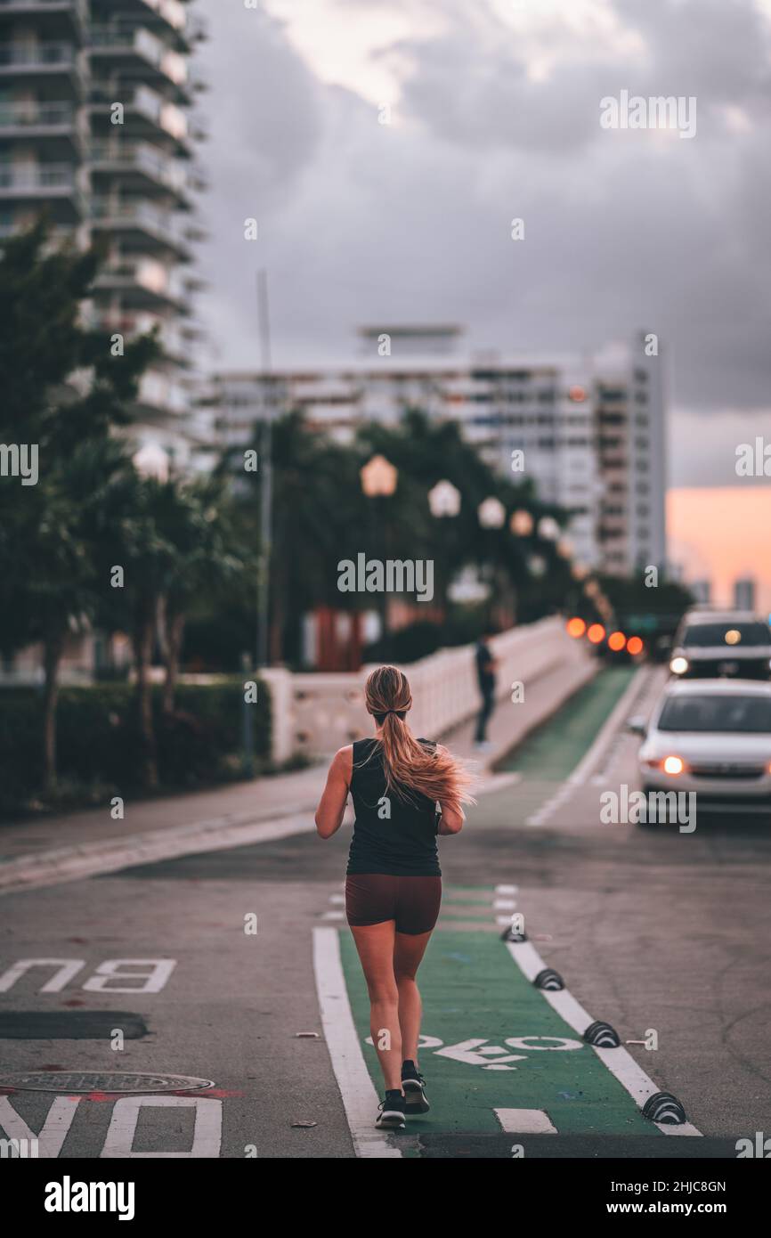 Vertical back view of a female running on a sidewalk in the evening ...