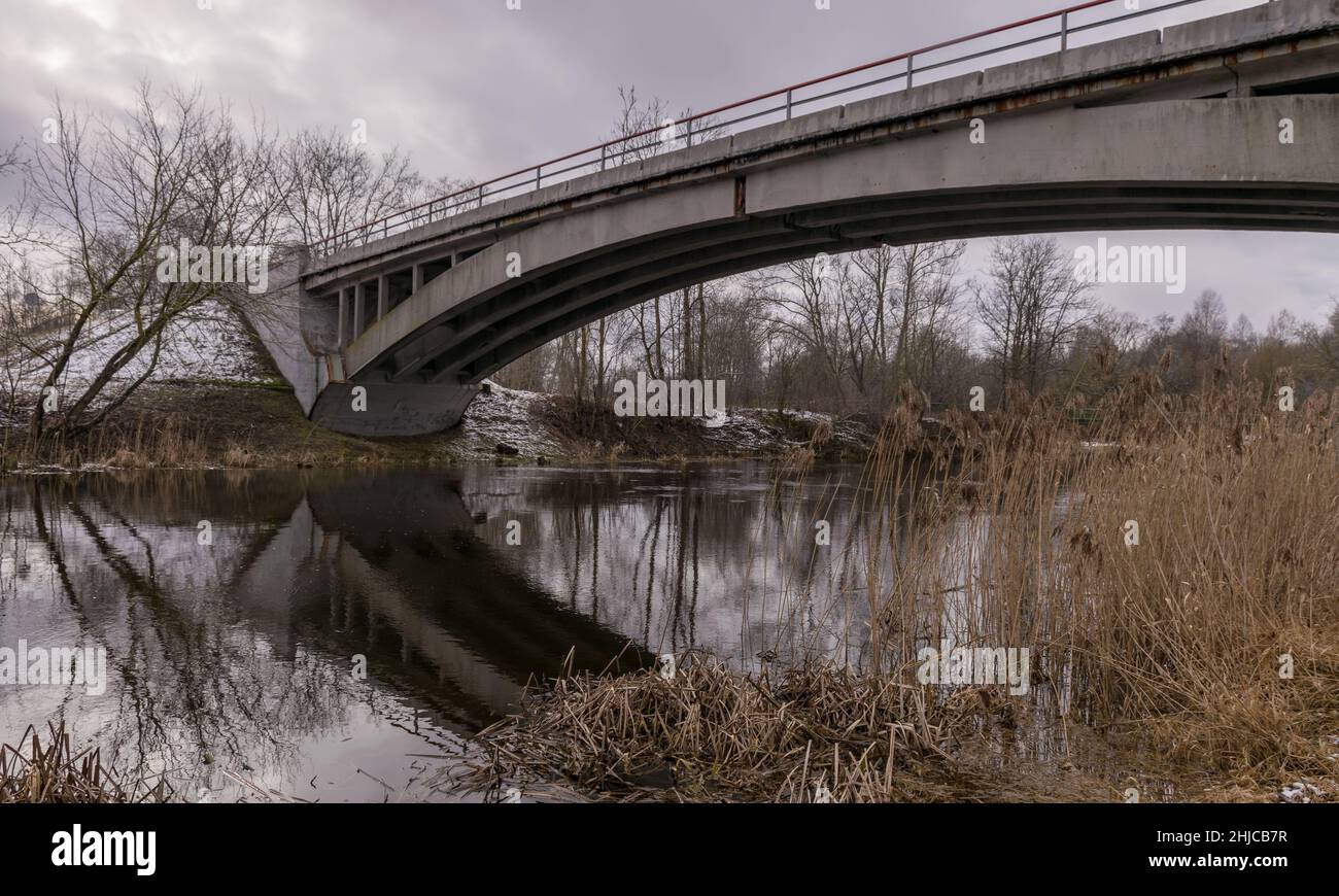 concrete arched bridge over a small and wild river, overgrown with ...