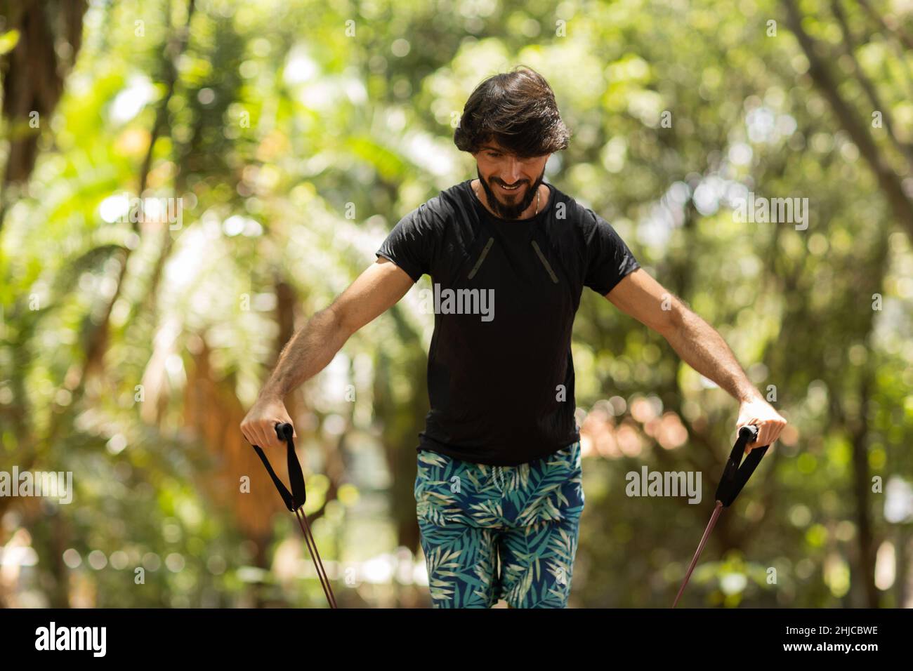 Strong man guy working out with elastic rubber bands at a park outdoors ...