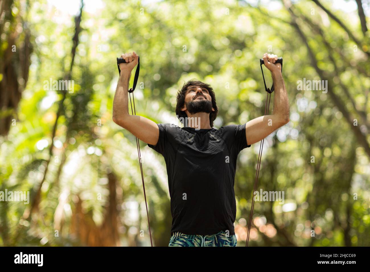 Strong man guy working out with elastic rubber bands at a park outdoors ...
