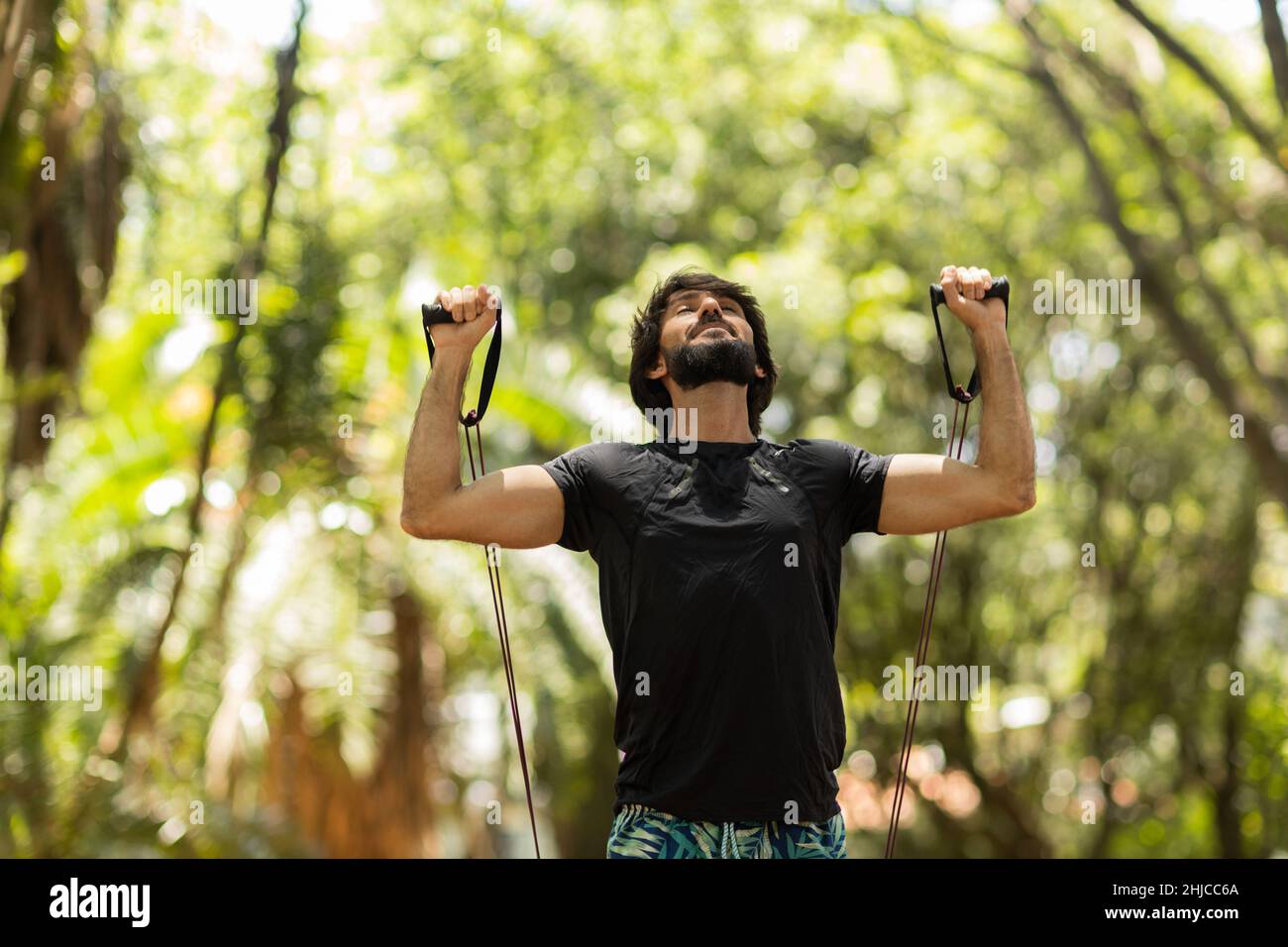 Strong man guy working out with elastic rubber bands at a park outdoors ...