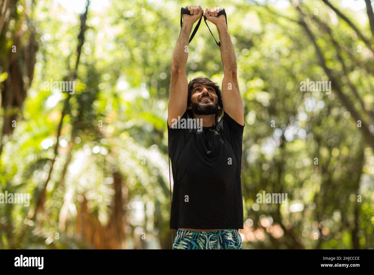 Strong man guy working out with elastic rubber bands at a park outdoors ...