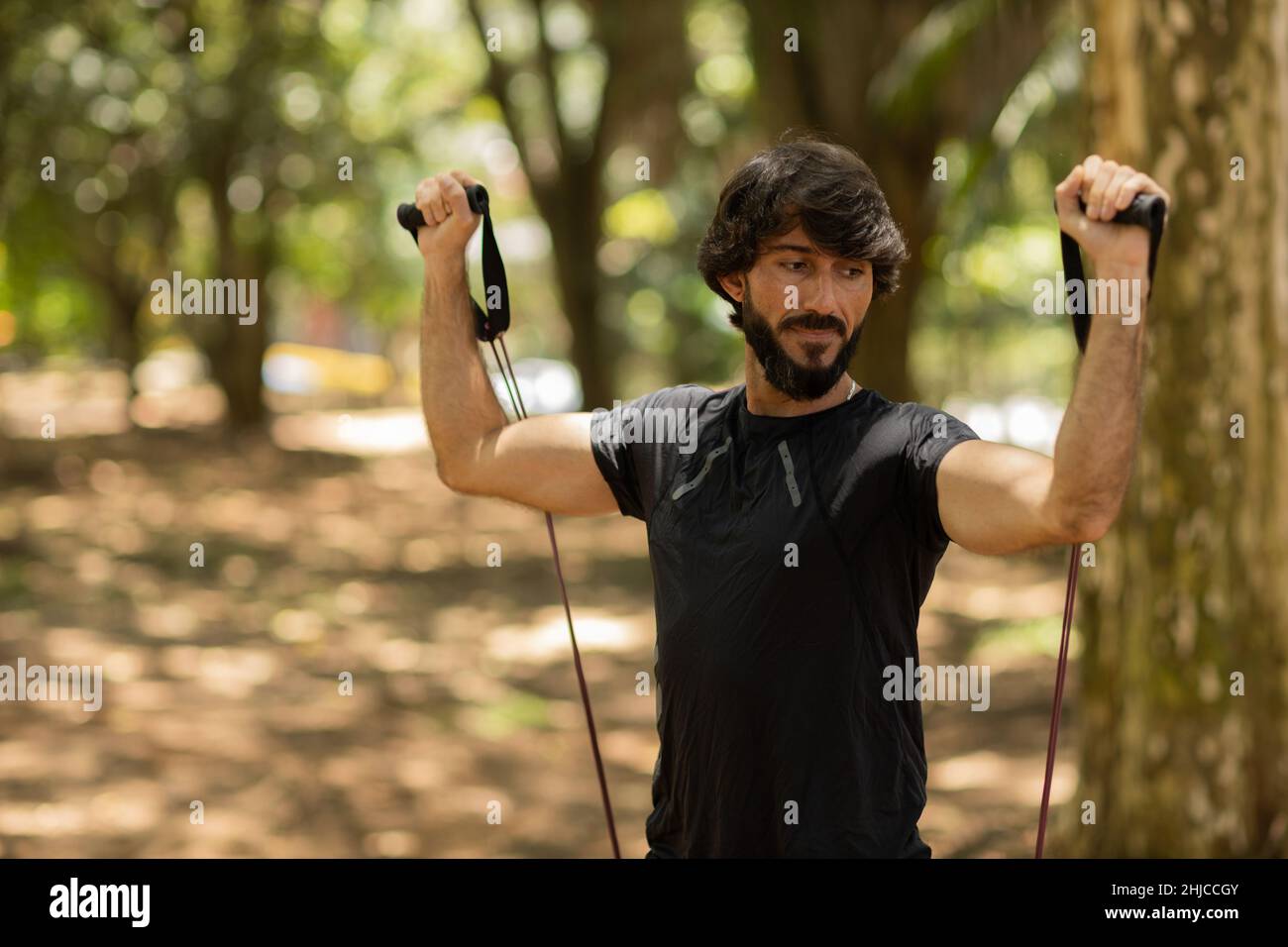 Strong man guy working out with elastic rubber bands at a park outdoors ...
