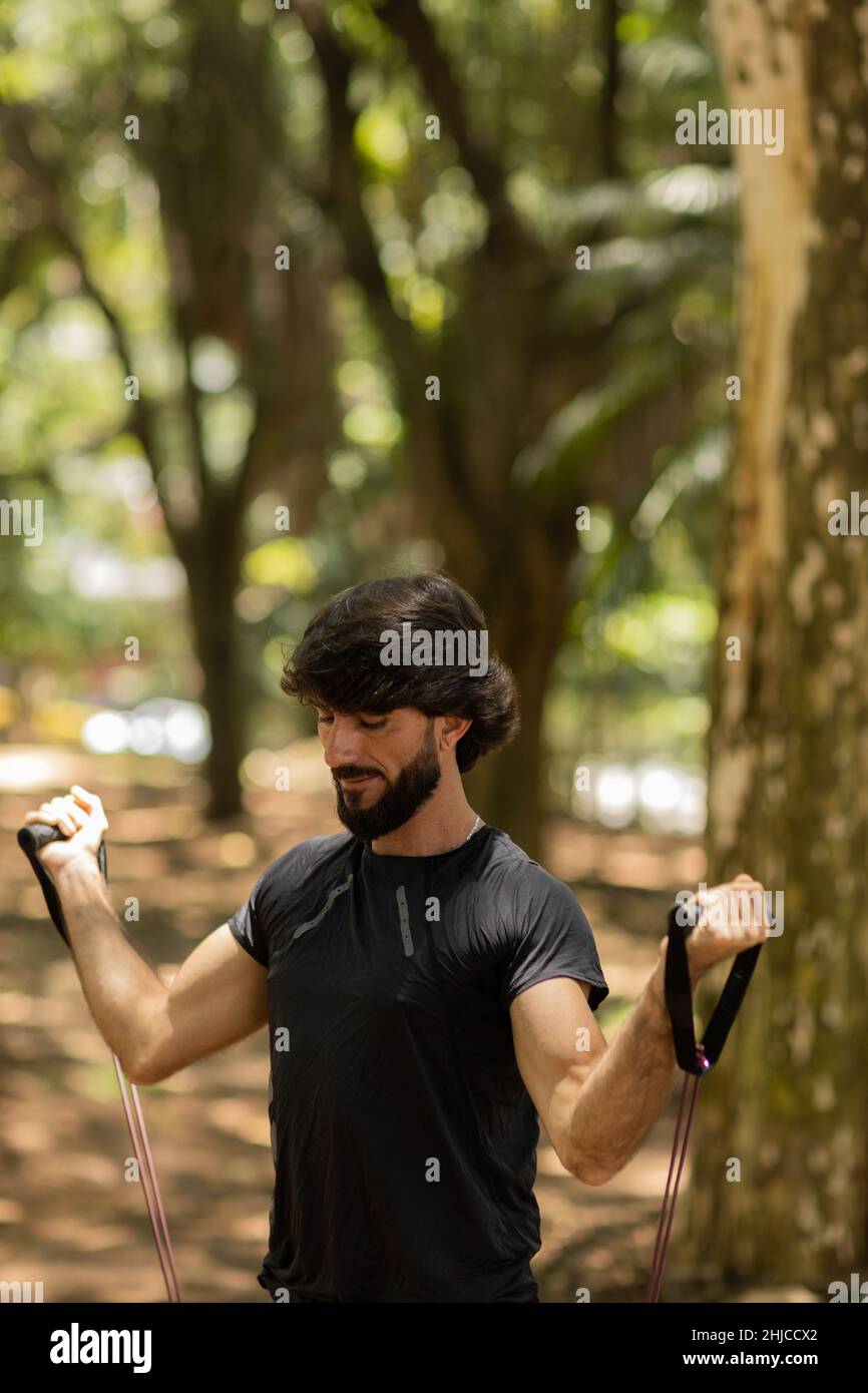 Strong man guy working out with elastic rubber bands at a park outdoors ...