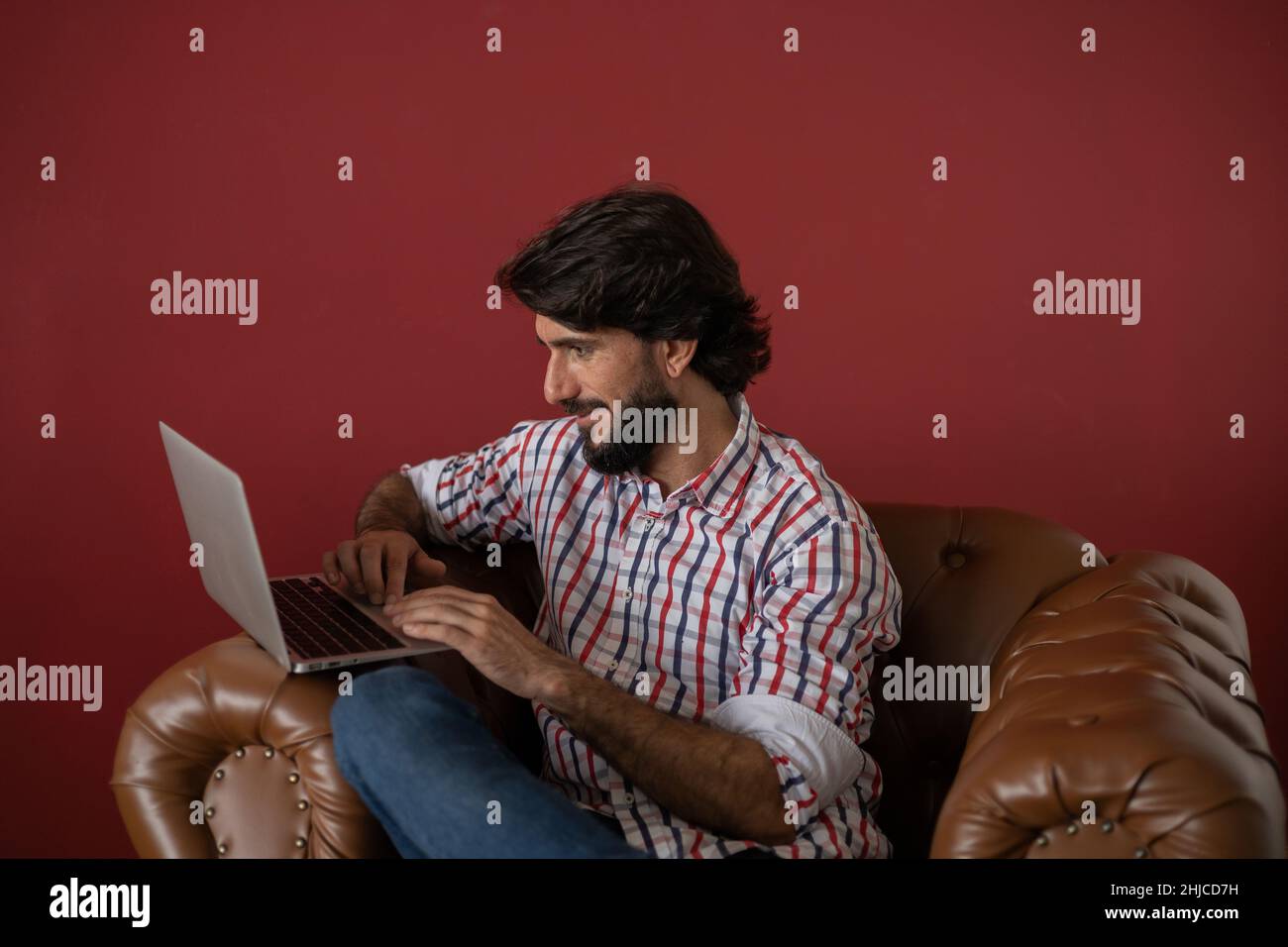 Young business man working at home with laptop on a brown arm chair ...