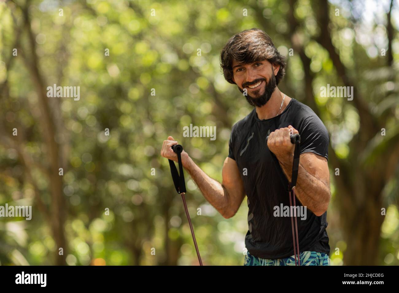 Strong man guy working out with elastic rubber bands at a park outdoors ...