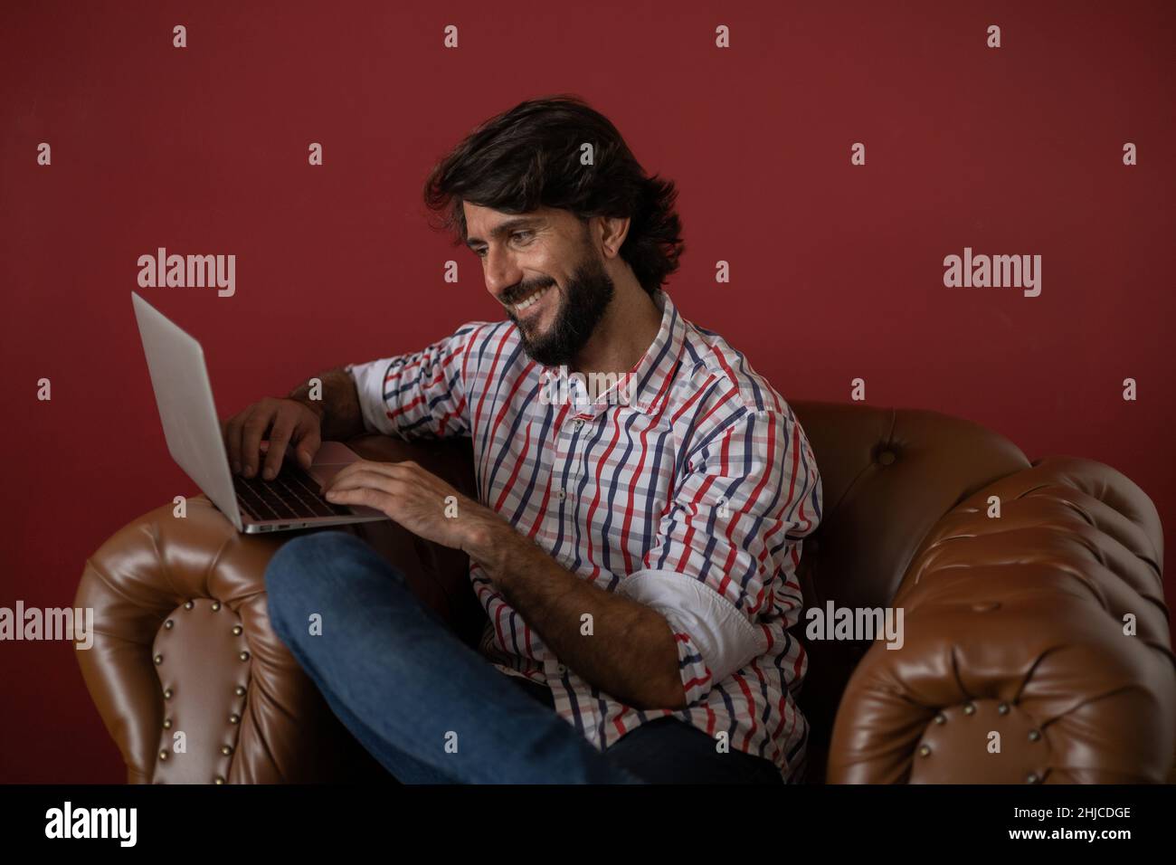 Young business man working at home with laptop on a brown arm chair ...