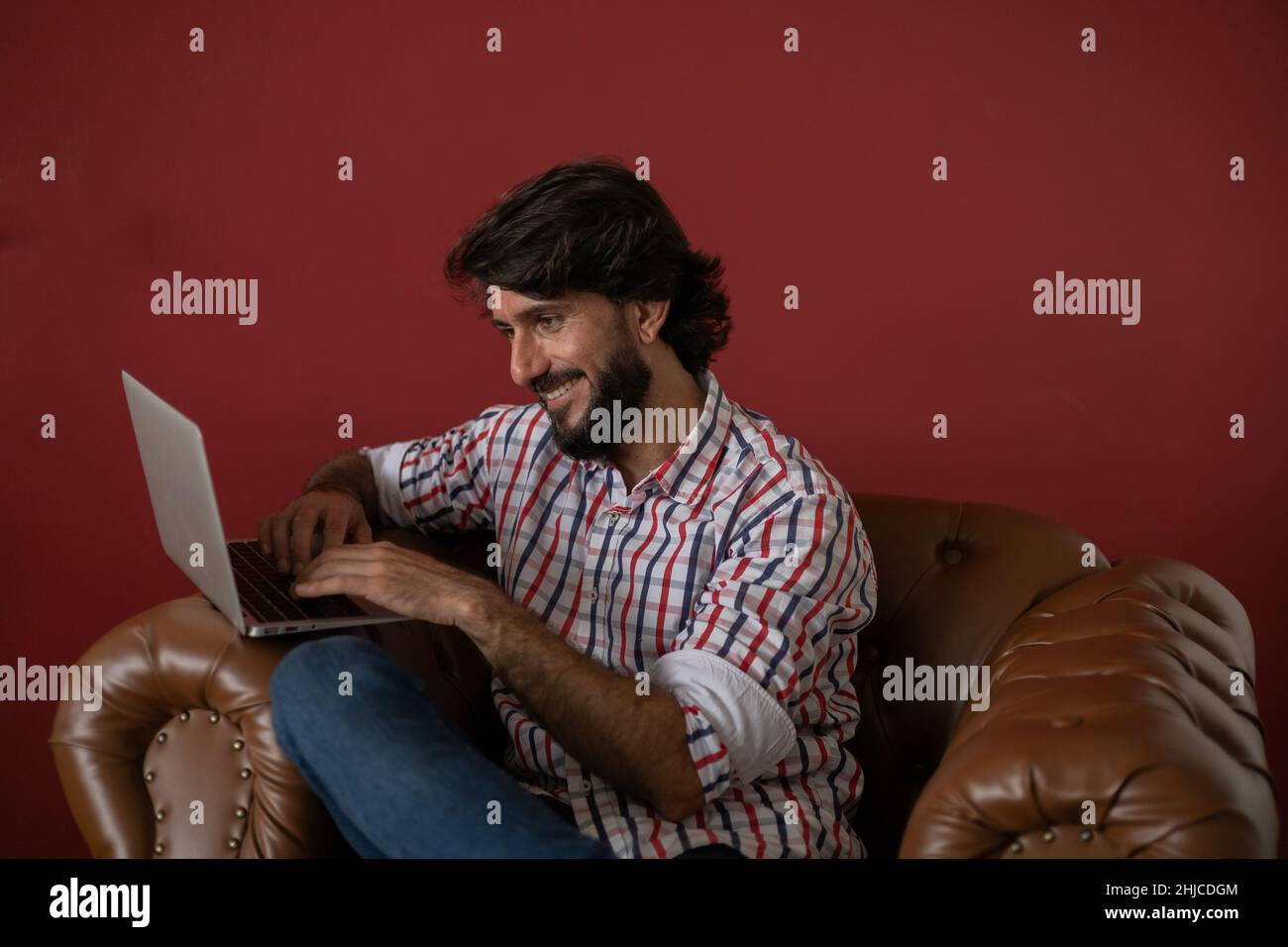 Young business man working at home with laptop on a brown arm chair ...