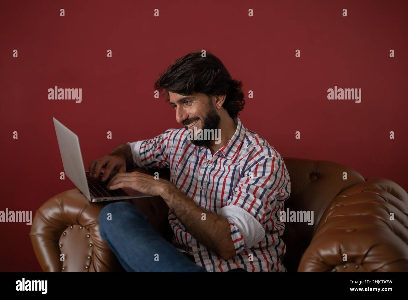 Young business man working at home with laptop on a brown arm chair ...