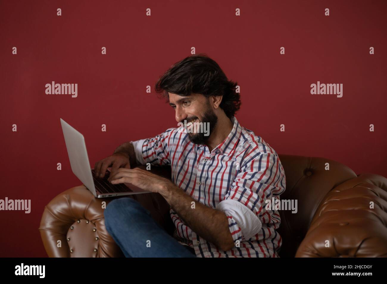 Young business man working at home with laptop on a brown arm chair ...