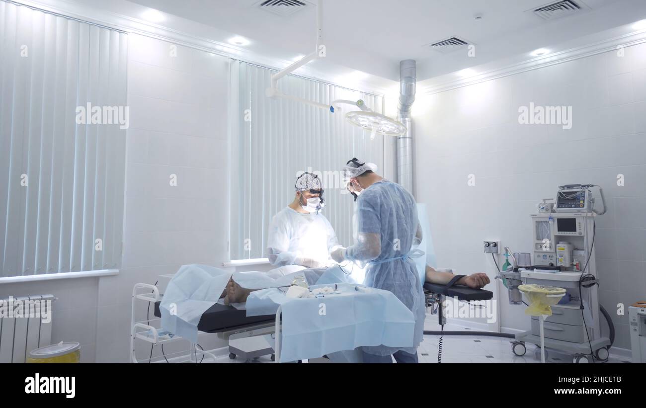 Surgeons operate on patient under anesthesia. Action. Two professional ...