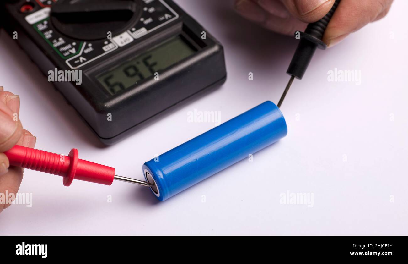 18650 blue battery, multimeter red and black poles in the hands of man ...