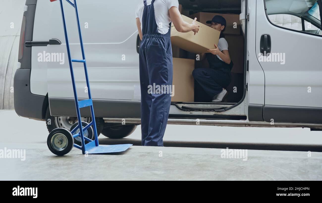 Smiling delivery woman in car holding carton box near colleague ...