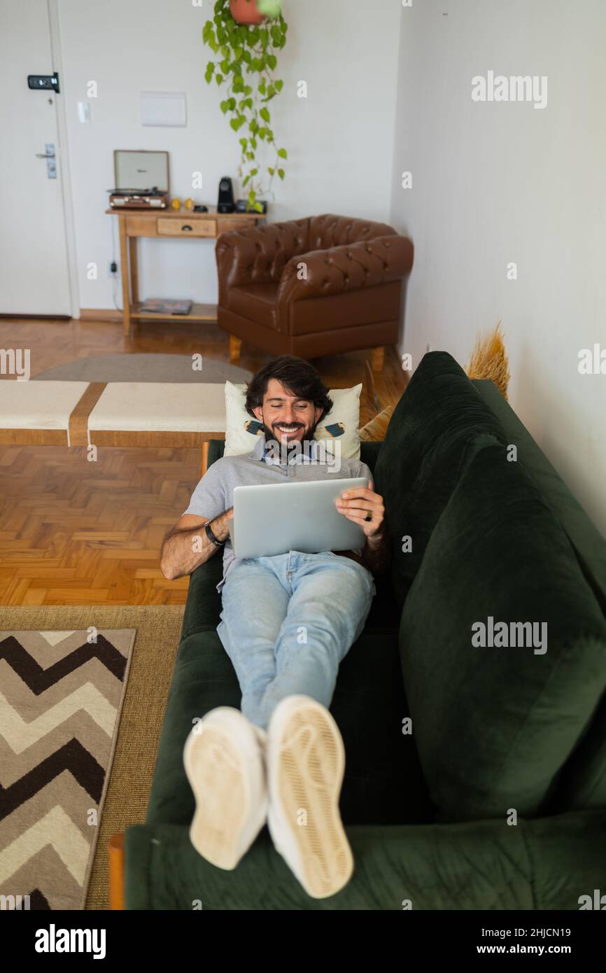 Young business man working at home from his living room couch with ...