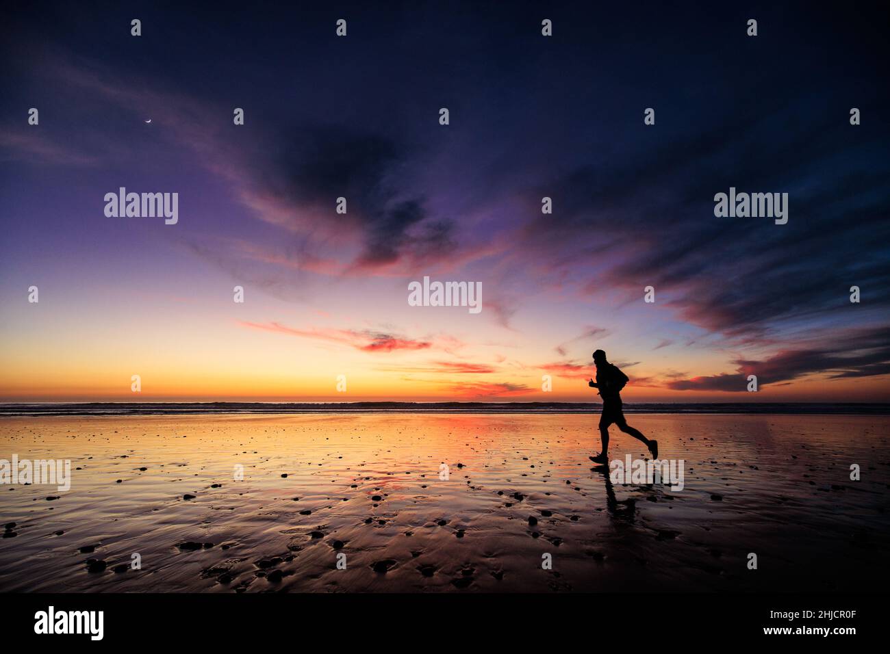 A runner reflected on a glossy beach under a colorful winter sunset at ...