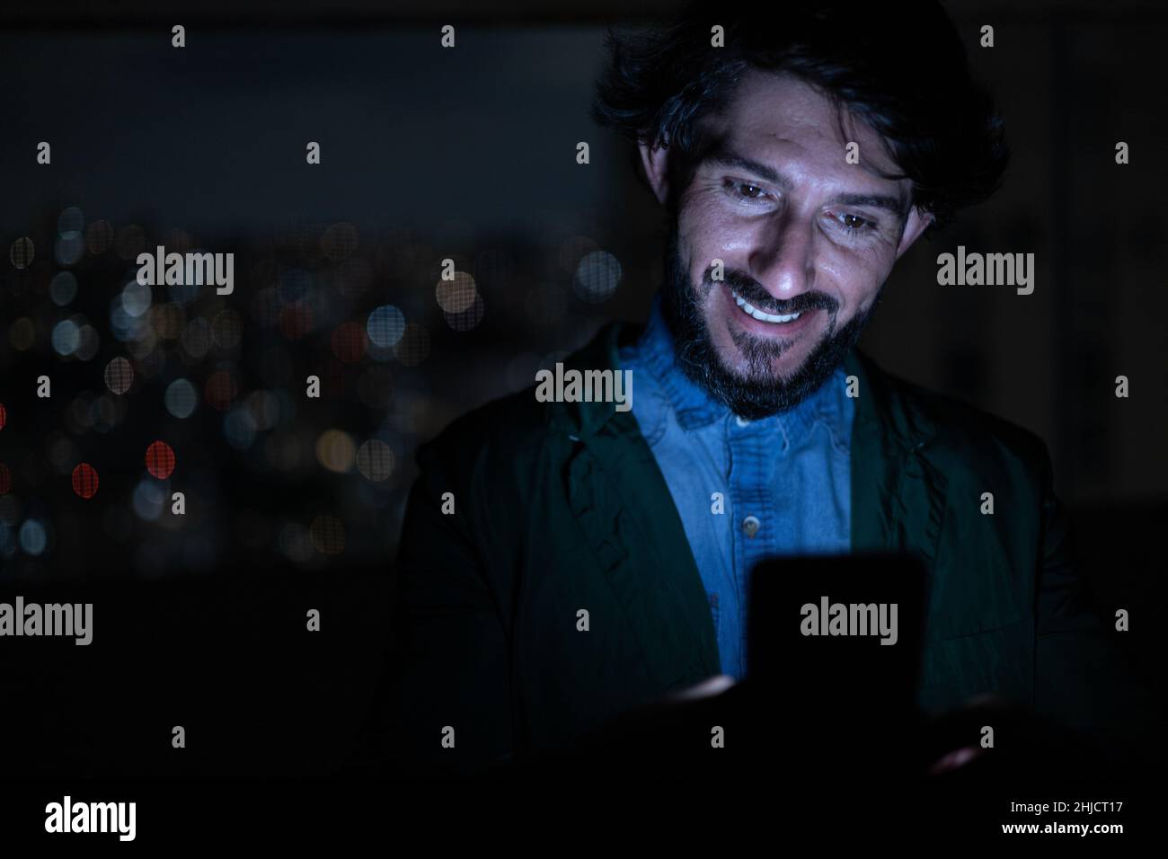 Front view of young man using a smartphone at night time with city view ...