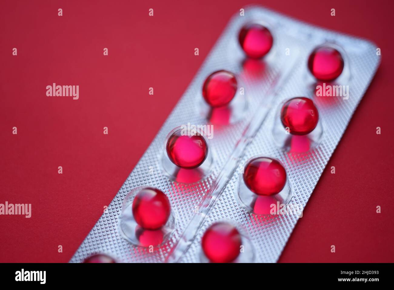 Red round pills vitamins capsules in a blister pack on a red table ...