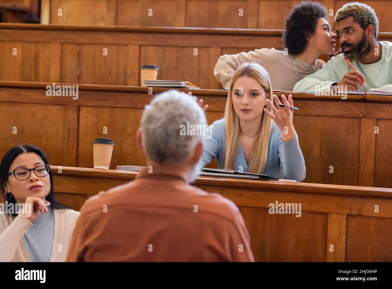 Multicultural students looking at blurred professor during lecture in ...