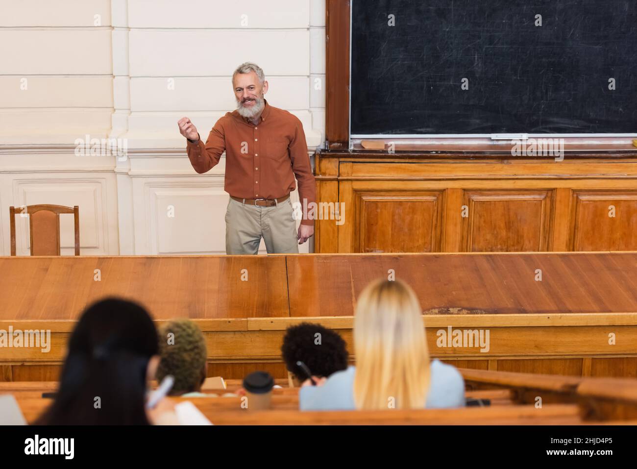 Smiling professor talking during lecture near blurred interracial ...