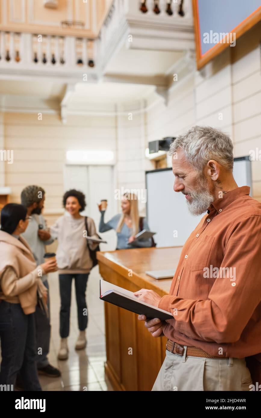 Middle aged professor holding notebook near interracial students in ...