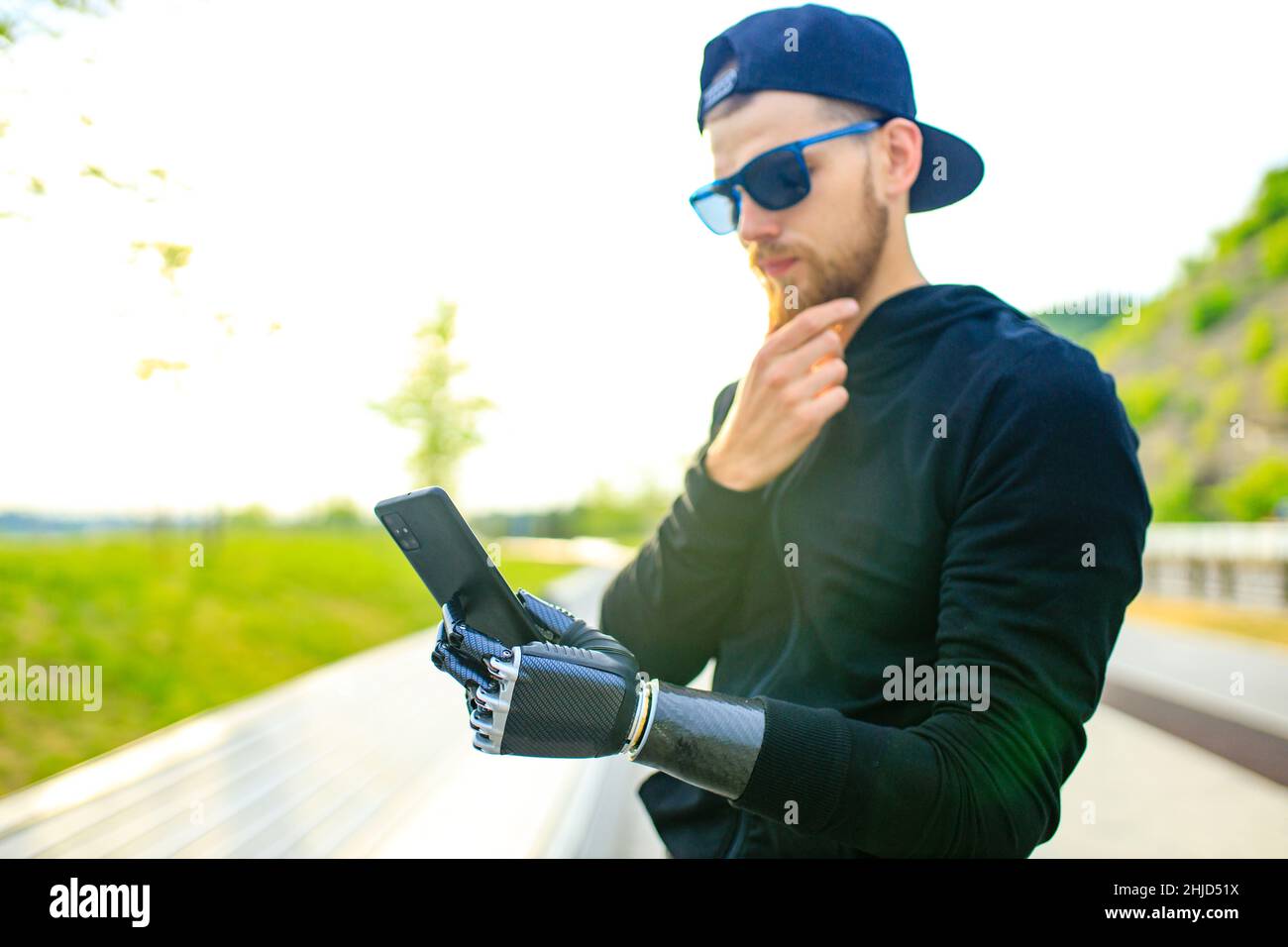 young bearded man with metal arm prosthetic outdoor looking at screen ...