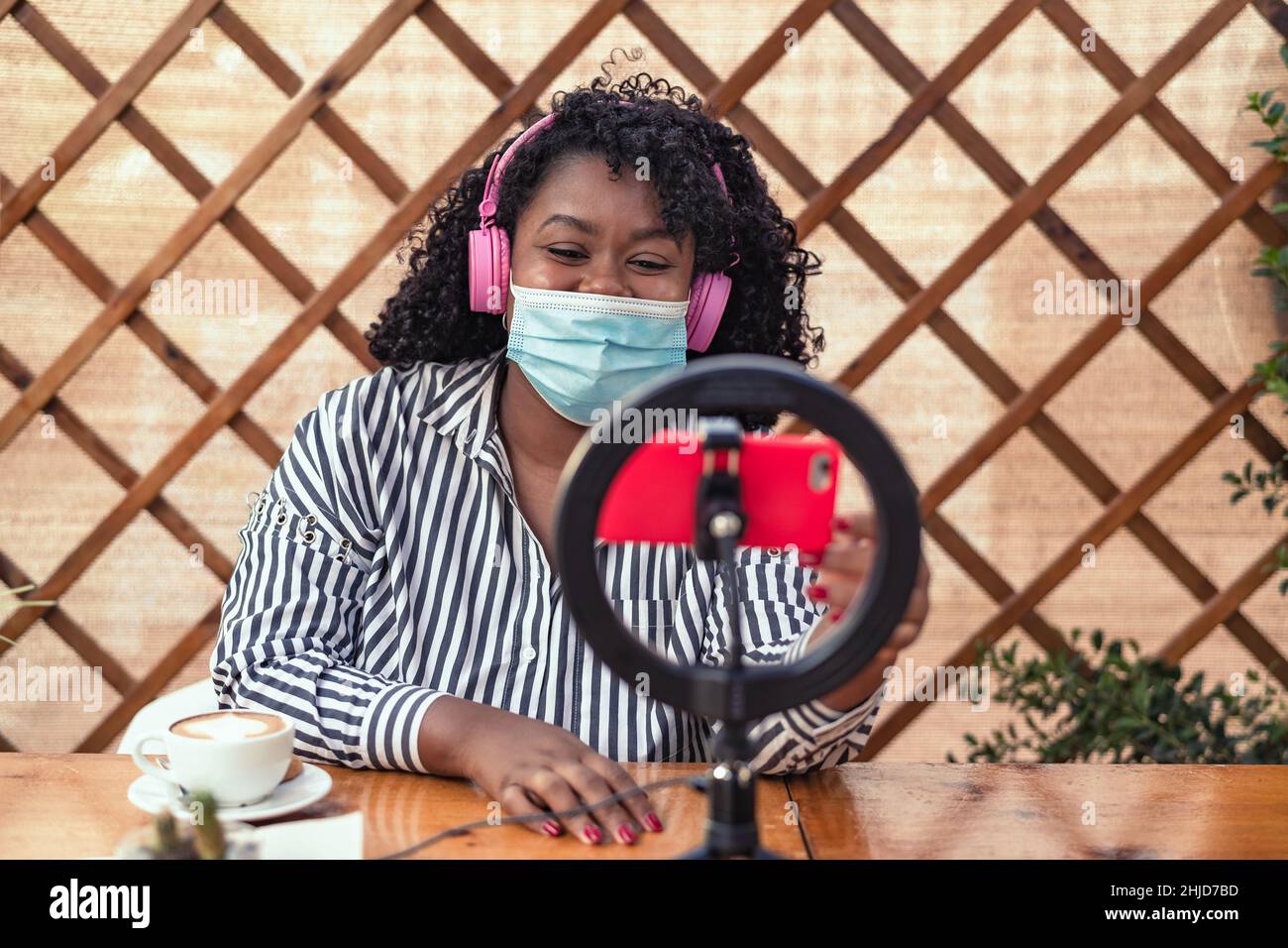 Happy latin woman wearing face mask vlogging online using smartphone ...