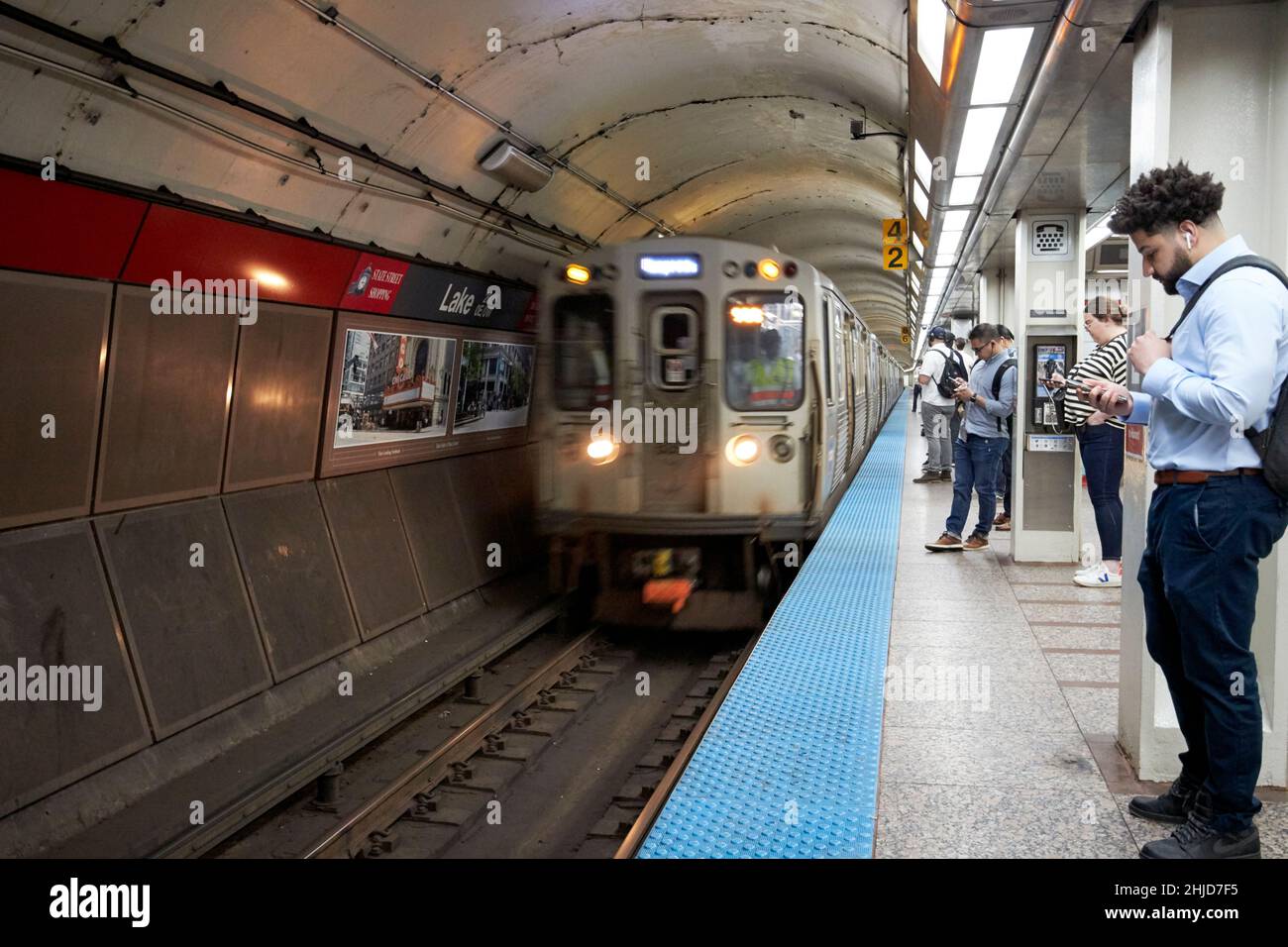 passengers looking down at phones as train approaches on long platform ...