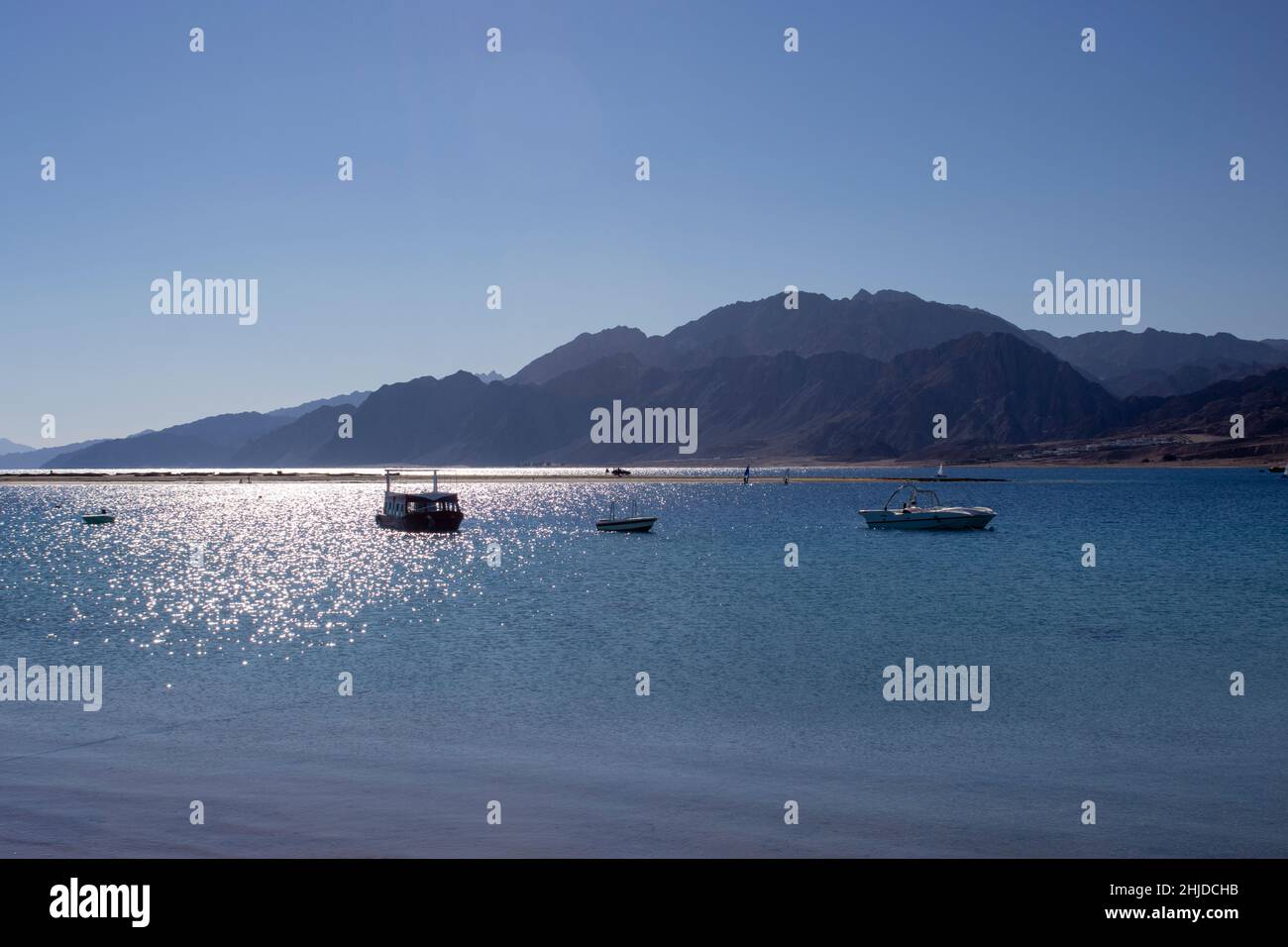 The sun reflecting on a beautiful blue lagoon in Dahab, Egypt. Boats in ...